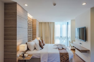 Quarto de hotel moderno com uma cama grande, televisão, escrivaninha e varanda com cortinas.