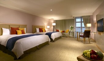 Quarto de hotel com duas camas, um sofá, uma televisão e uma cesta de frutas.
