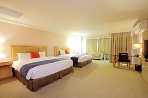 Quarto de hotel com duas camas, uma escrivaninha, uma cadeira e uma janela com cortinas.