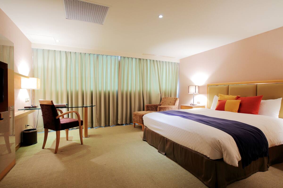 Quarto de hotel com cama, escrivaninha, cadeira e televisão.