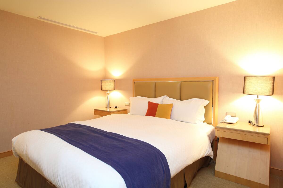 Quarto de hotel com uma cama grande, duas mesas de cabeceira com abajures e uma cabeceira.