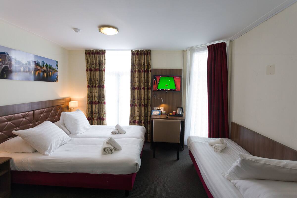 Quarto de hotel com duas camas, uma escrivaninha, uma televisão e um quadro na parede.