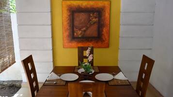 Mesa de jantar posta para dois, com acabamento em madeira, um vaso com flores e uma obra de arte emoldurada na parede.