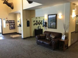 Um hall com sofá de couro, cabeça de veado montada, estante de livros e um quadro na parede.