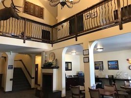 Um saguão de hotel com escadaria, lareira e área de refeições com mesas e cadeiras.