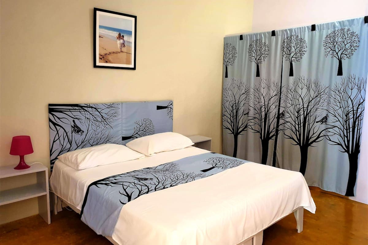 Quarto com uma cama, mesa de cabeceira, abajur vermelho e quadro na parede.