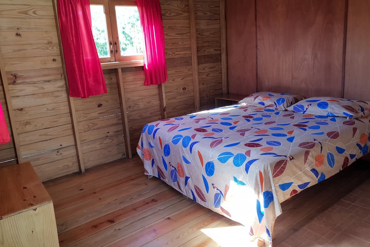 Quarto de cabana de madeira com cama, cortinas vermelhas e janela.