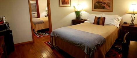 Quarto de hotel com uma cama grande, duas luminárias laterais, um espelho e piso de madeira.