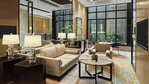 Um saguão moderno de hotel com um sofá, poltronas, uma mesa de centro e uma televisão.