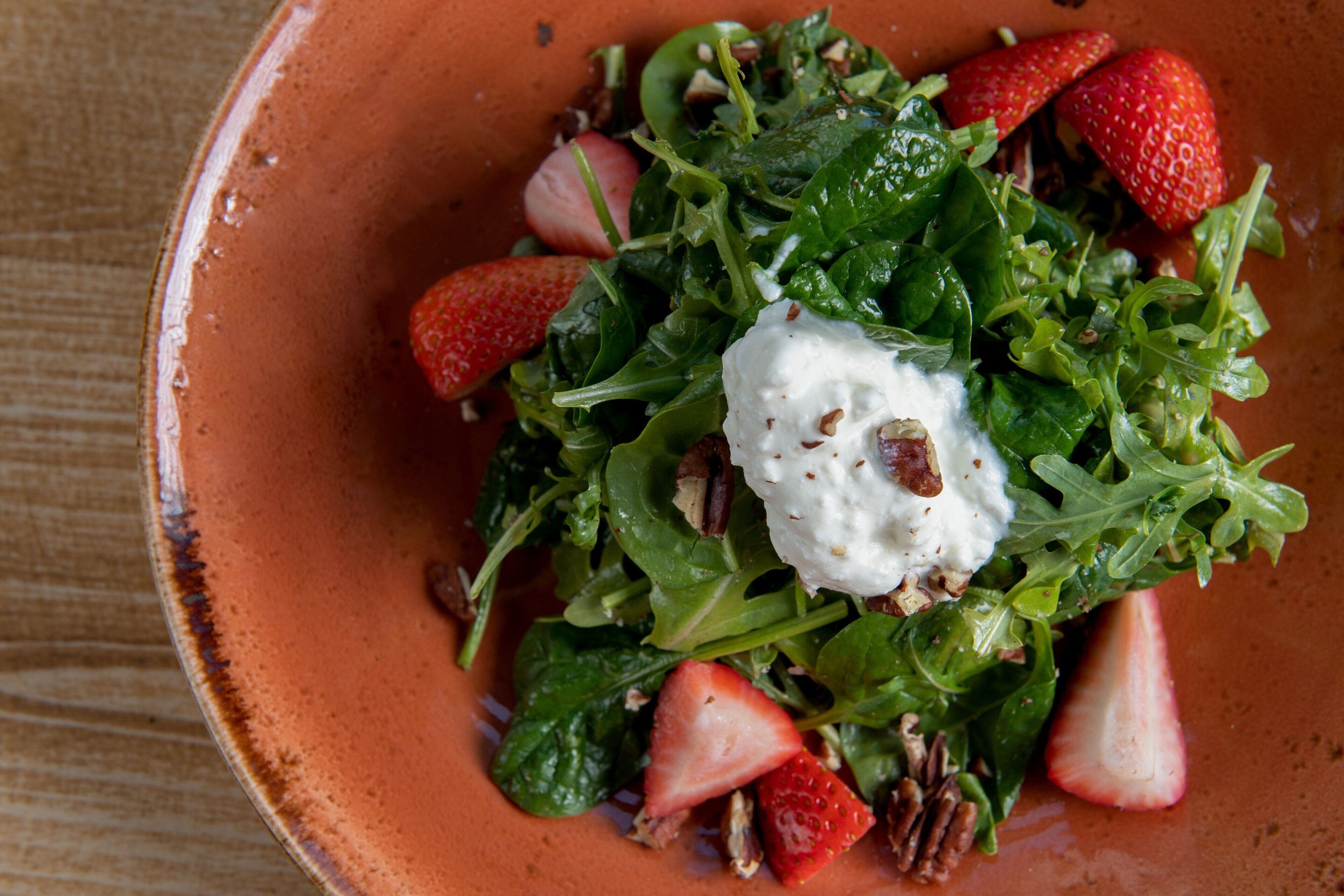 Salada com morangos e nozes pecan num recipiente de barro.