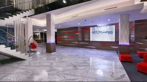 Um saguão moderno com piso de mármore, assentos vermelhos e uma tela grande exibindo 'ASTONLAMPUNG'.