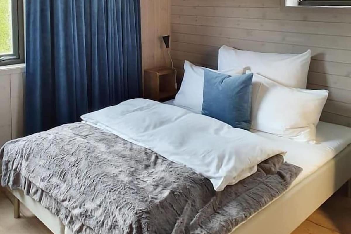 Quarto com cama, janela com cortinas e luminária fixada na parede.