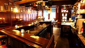 Uma área de bar com balcões de madeira, banquetas e uma variedade de garrafas e copos.