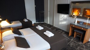 Quarto de hotel com duas camas, uma escrivaninha, uma cadeira, uma televisão e um espelho.