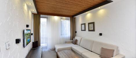 Uma sala de estar moderna com teto de madeira, um sofá bege, uma mesa de centro de madeira e uma janela grande com cortinas.