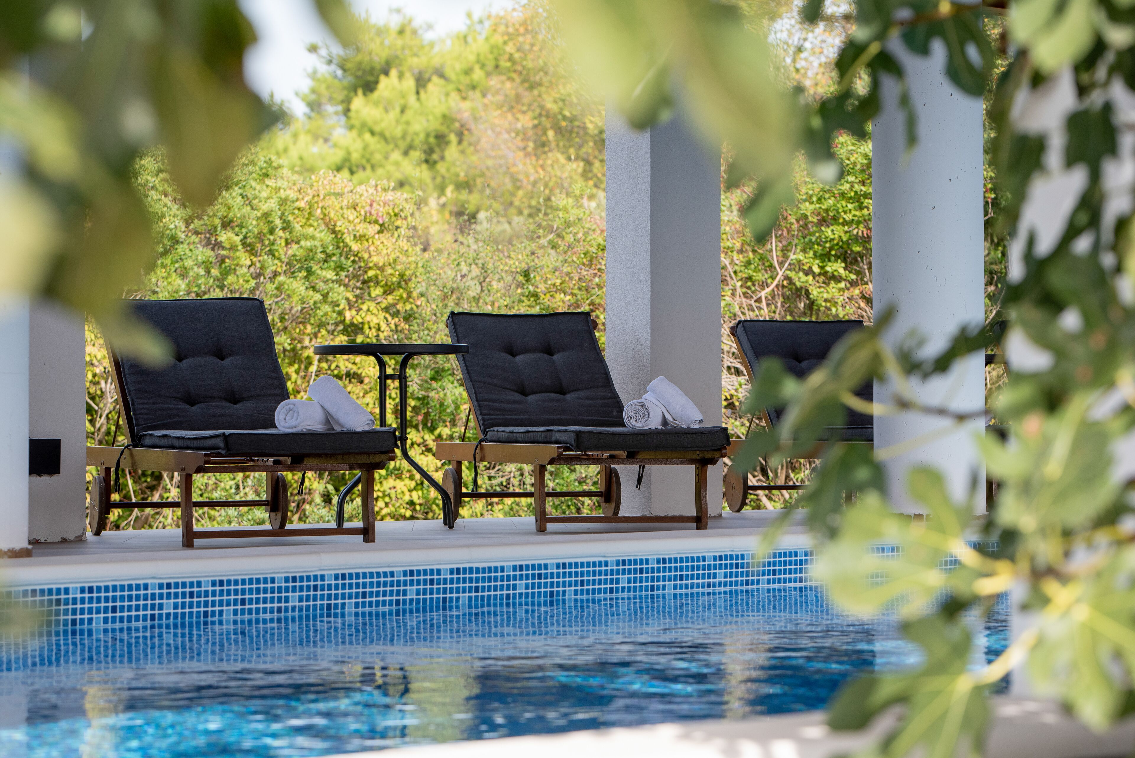 Uma área à beira da piscina com espreguiçadeiras e uma piscina em mosaico.