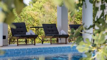 Uma área à beira da piscina com espreguiçadeiras e uma piscina em mosaico.