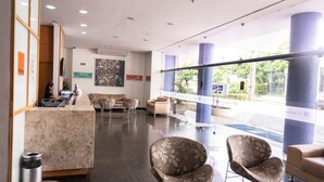 Uma área de recepção moderna com balcão de mármore, assentos confortáveis e amplas janelas com vista para o exterior.