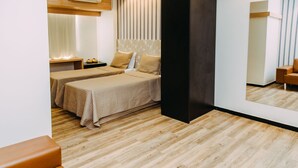 Quarto de hotel moderno com duas camas, piso de madeira, um espelho grande e um pequeno espaço de estar.