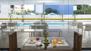 Espaço de refeições com mesa posta para o café da manhã, com vista para uma piscina.