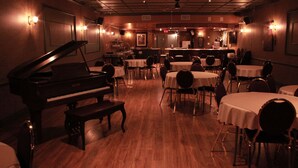 Um restaurante com um piano de cauda, soalho de madeira e mesas com toalhas brancas.