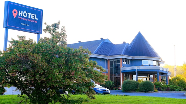 Um hotel com design moderno, apresentando uma placa de identificação, um gramado bem cuidado e uma área de estacionamento.