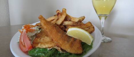 Um prato de peixe com batatas fritas, uma salada, uma fatia de limão e um copo de vinho branco.
