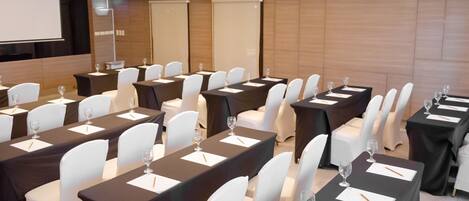 Uma sala de conferências com fileiras de mesas, cada uma com cadeiras brancas e toalhas pretas.
