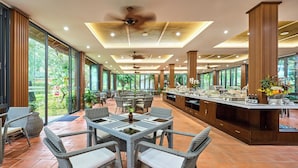Um espaço interno amplo com uma grande mesa de jantar, cadeiras de vime, uma ilha central com balcão e janelas grandes que oferecem vista para o exterior.