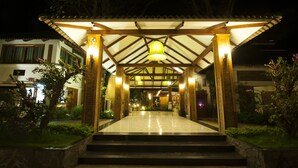 Uma entrada coberta com degraus que levam a um edifício, cercada por vegetação e iluminada por luzes pendentes.