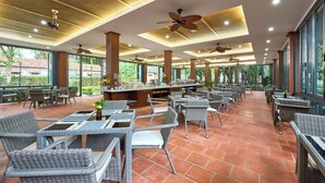 Uma área de refeições ao ar livre ampla, com mobiliário de vime e um bar central.