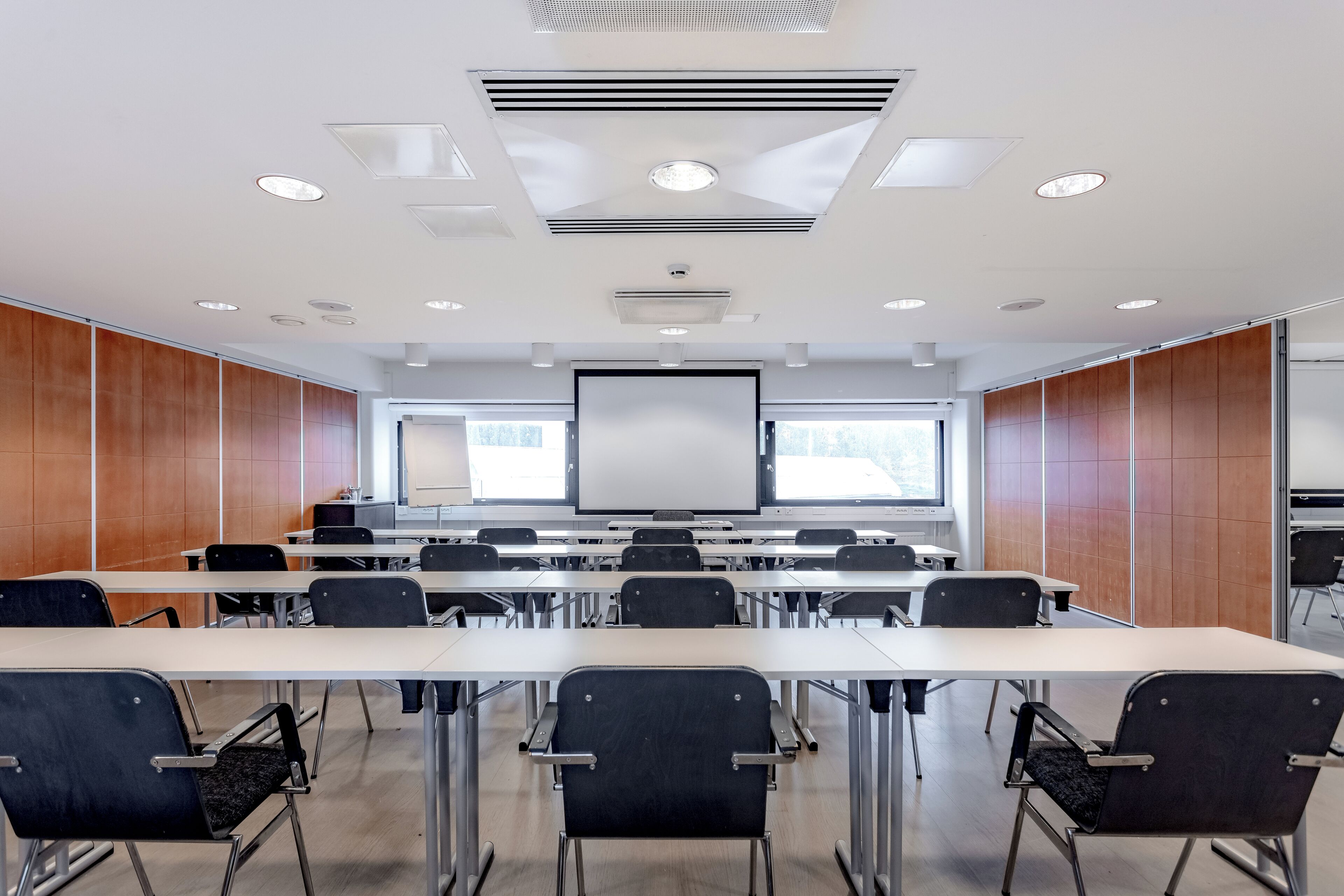 Uma sala de conferências com uma mesa comprida, cadeiras, uma tela de projetor e uma janela grande.