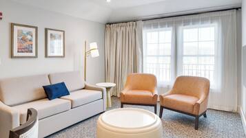 Quarto de hotel com sofá, duas poltronas, uma mesa redonda pequena e uma luminária. Há duas quadros decorativos na parede.