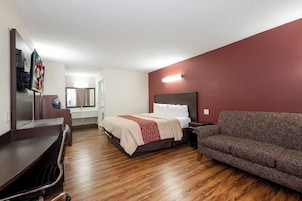 Quarto de hotel com cama, sofá, escrivaninha e televisão.