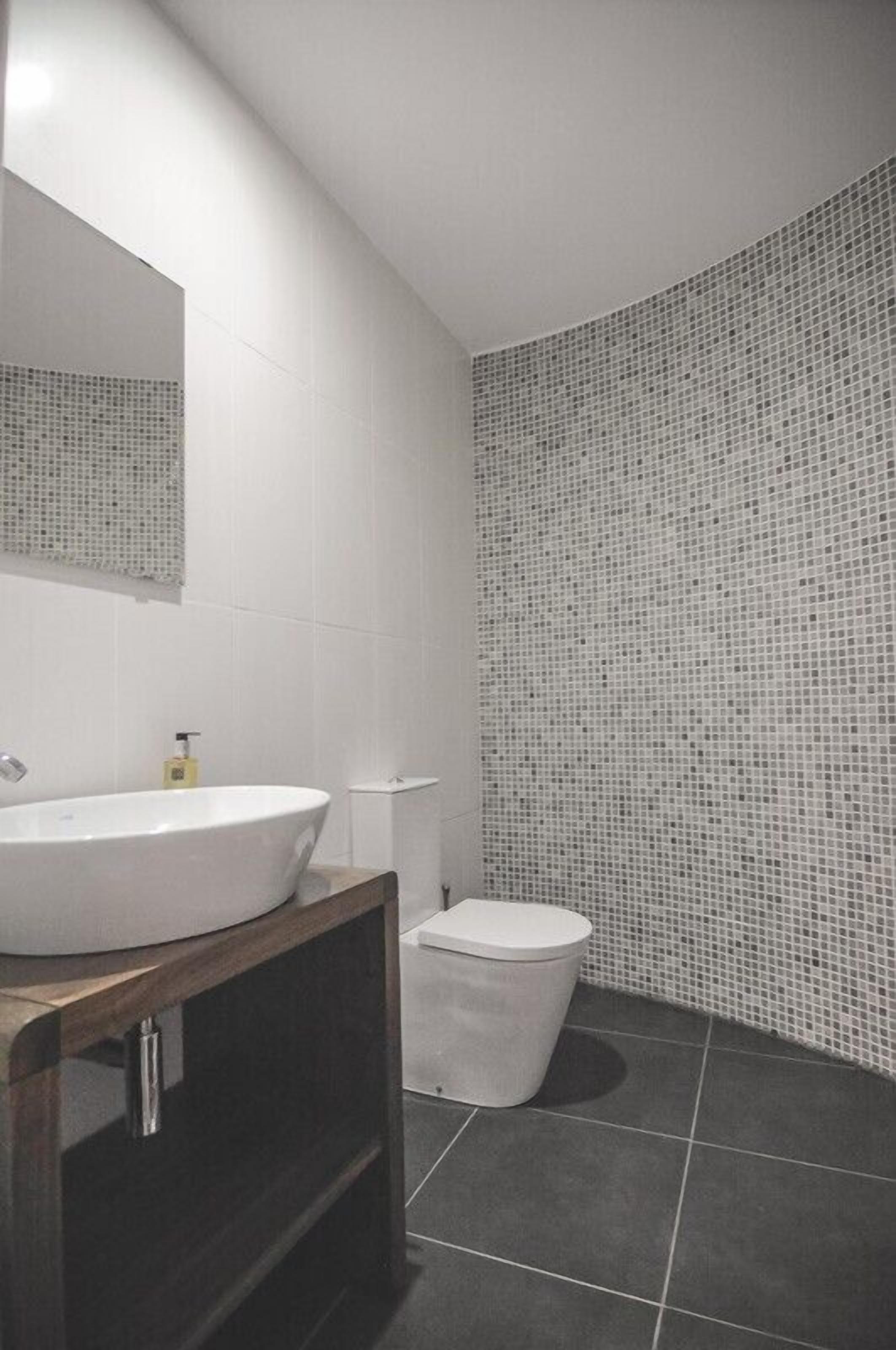 Um banheiro com pia branca, vaso sanitário e parede de chuveiro revestida com azulejos.