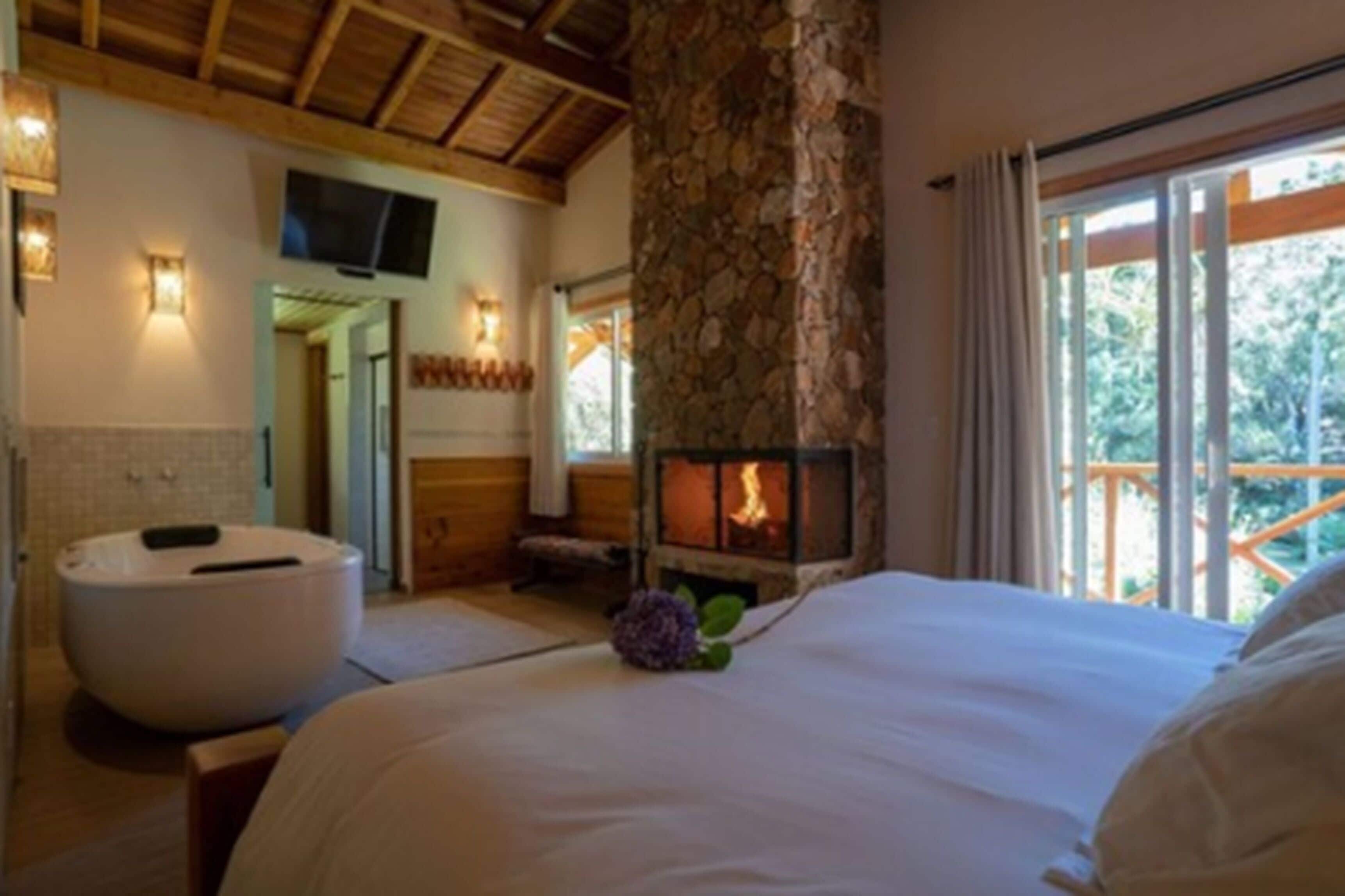 Quarto com lareira de pedra, uma banheira grande e vista para o exterior.