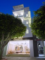 Um hotel com uma loja boutique no andar térreo, grandes janelas e uma árvore na frente.