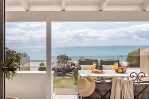 Uma varanda com mesa posta para o café da manhã, com vista para a costa.