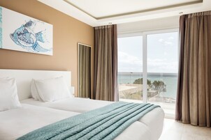 Quarto de hotel com uma cama grande, vista para o oceano e um quadro na parede.