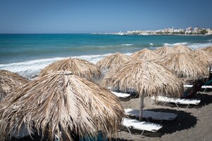 Uma praia com guarda-sóis de palha e espreguiçadeiras.