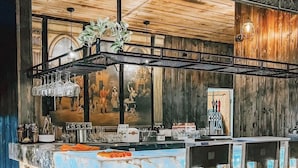 Uma área de bar com balcão de pedra, banquetas e um mural na parede.