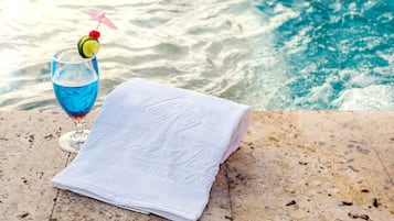 Toalha branca com a palavra 'HOTEL' estampada, colocada sobre uma superfície de pedra junto a uma piscina com água azul cristalina.