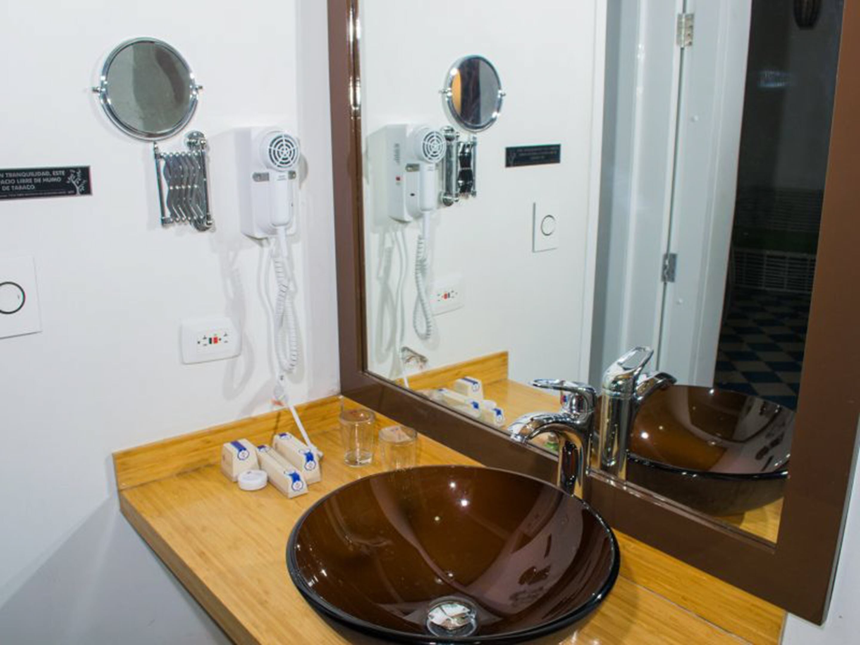 Casa de banho com toucador de madeira, um espelho grande, uma sanita redonda e um secador de cabelo fixado na parede.
