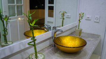 Um banheiro com um espelho grande, uma pia em vaso amarelo e duas plantas em vasos.