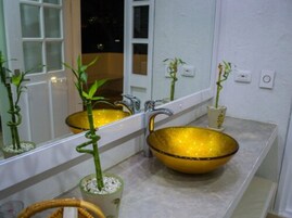 Um banheiro com um espelho grande, uma pia em vaso amarelo e duas plantas em vasos.
