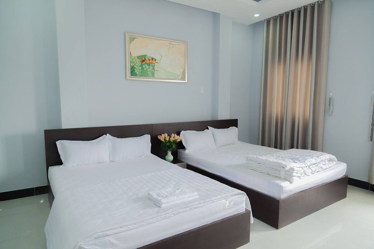 Quarto de hotel com duas camas, um quadro na parede e uma janela com cortinas.