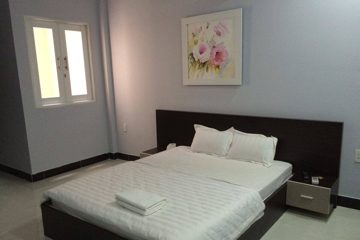 Quarto com cama, mesa de cabeceira, gaveta, janela e pintura na parede.