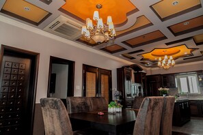 Uma sala de jantar com mesa de madeira escura, cadeiras acolchoadas e um lustre.