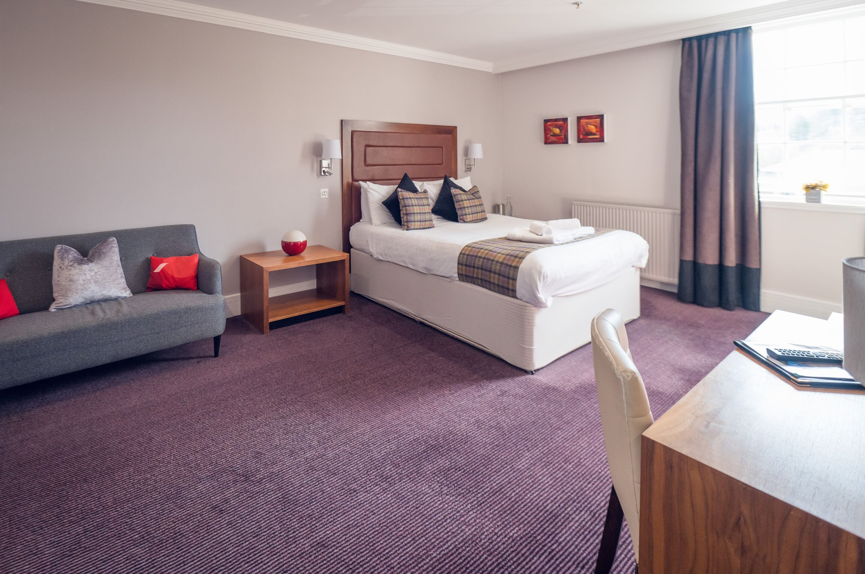 Quarto de hotel com cama, sofá, mesa pequena e cadeira.