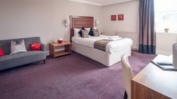 Quarto de hotel com cama, sofá, mesa pequena e cadeira.